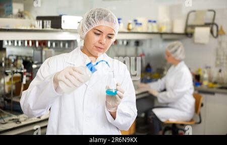 Efficient female lab technician working with reagents in test tubes ...