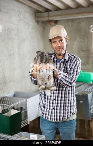 Man farmer with rabbit in her hands on her farm. Farmer takes care of ...