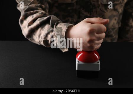 Serviceman pressing red button of nuclear weapon at black table ...