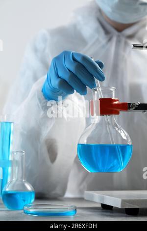 Scientist taking sample of light blue liquid and test tubes in ...