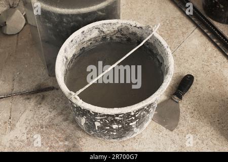Bucket of adhesive mix and spatula on floor indoors Tiles installation ...