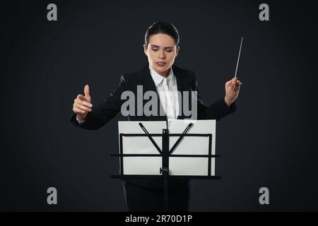 Professional conductor with baton and note stand on grey background ...