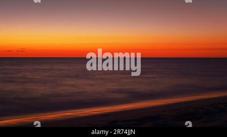 Vibrant orange red sky reflecting in calm ocean after sunset. Minimal ...