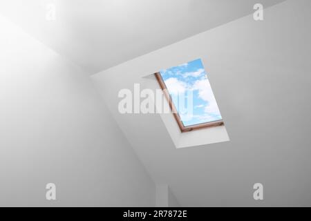 Skylight roof window and lamps on slanted ceiling in attic room, low ...