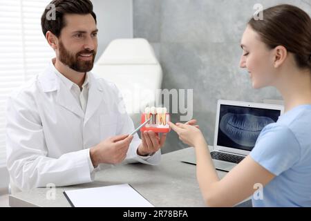 Doctor showing patient educational model of dental implant in clinic ...