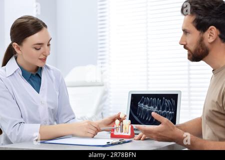 Doctor showing patient educational model of dental implant in clinic ...