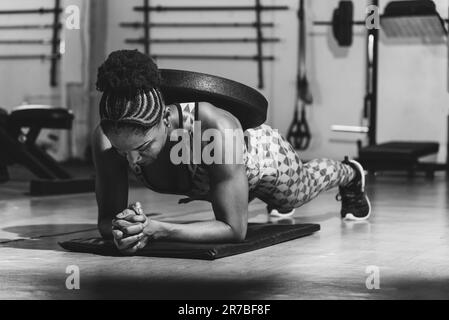 An athletic female fitness enthusiast engaging in a weighted planking ...