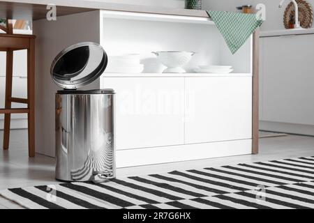Opened metallic trash bin near table in interior of modern kitchen ...
