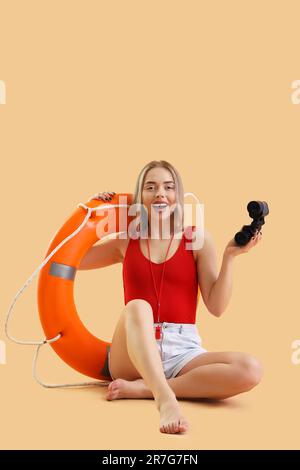 Female lifeguard with binoculars and ring buoy shouting into megaphone ...
