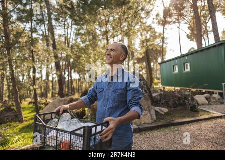 Mature man carrying crate with separated waste in garden Stock Photo ...