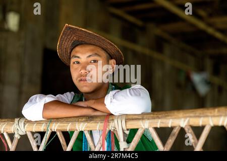 Teenager from galo tribe in traditional clothes with traditional hat on his head posing infront ...