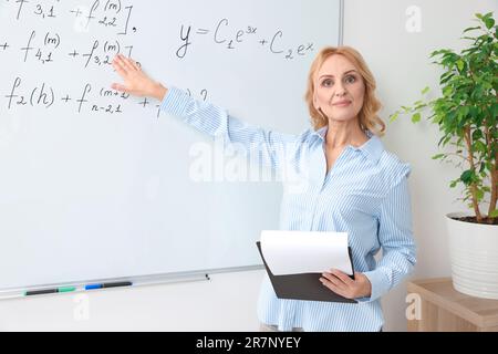 Professor with clipboard giving lecture near whiteboard in classroom ...