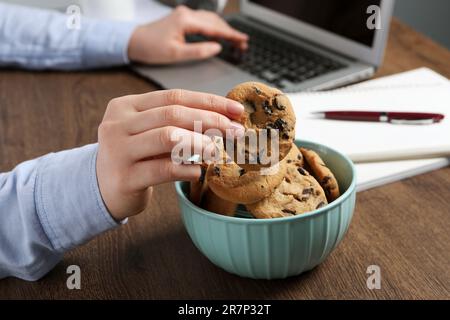 Office worker taking chocolate chip cookie from jar at workplace ...