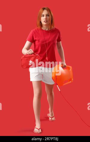 Female lifeguard with rescue buoy and first aid kit on red background ...
