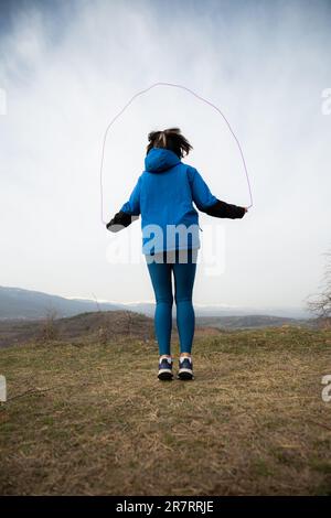 Amazing and active woman is doing a jumping rope exercise in the forest ...