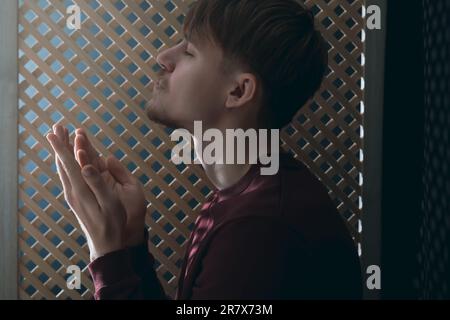 Man praying during confession near wooden window in booth. Space for ...