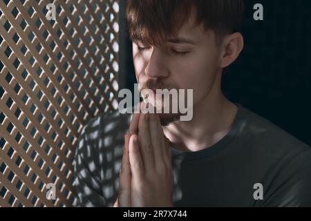 Man praying during confession near wooden window in booth. Space for ...