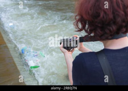 Female photographer photographing garbage in the river, plastic bottles ...