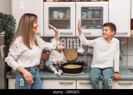 Mom and her children in the kitchen with pasta in the pan for dinner ...