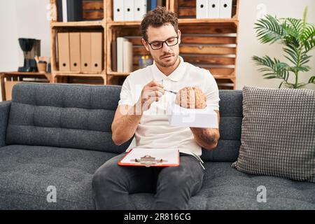 Handsome hispanic man holding brain working at psychology clinic ...