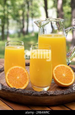 Orange juice in glasses and pither with sliced oranges outdoors on ...