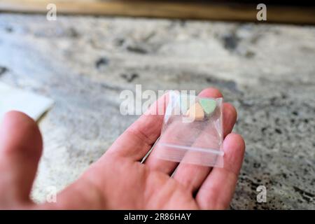 Hand holding Tesla ecstasy pills in orange, green, and blue color ...
