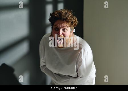Young deranged man in straitjacket biting pillow while lying on bed by ...