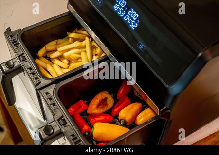 Dual-compartment air fryer with one drawer open to reveal french fries ...