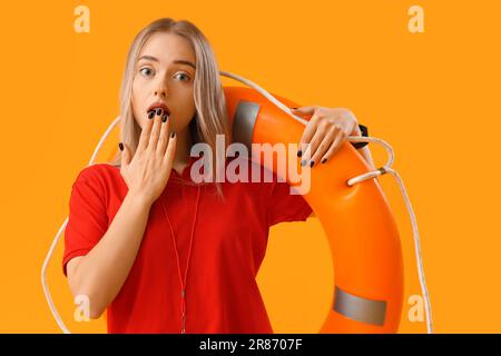 Shocked female lifeguard with ring buoy pointing at something on pink ...