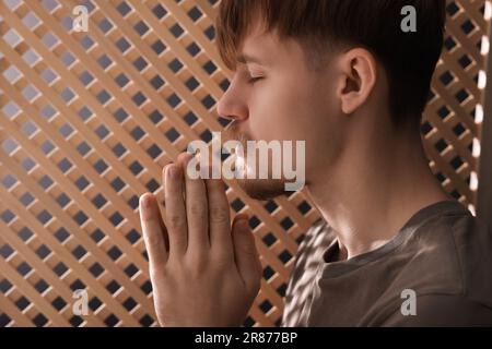 Man praying during confession near wooden window in booth Stock Photo ...