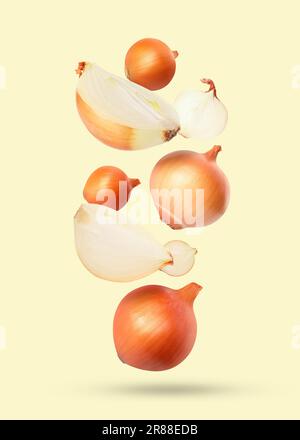 Cut and whole onions falling on beige background Stock Photo - Alamy