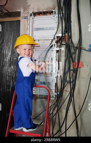 Little boy electrician in safety helmet holding electrical wires while ...
