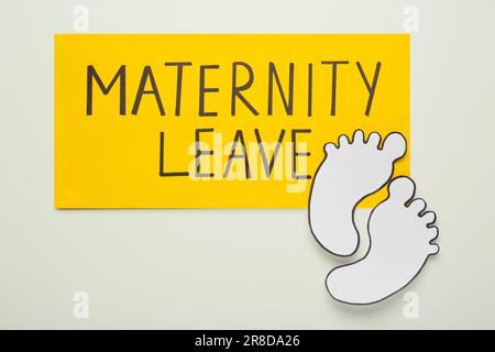 Note with words Maternity Leave and paper cutout of baby feet on orange ...