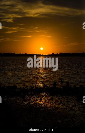 Captivating sunset over the tranquil sea in Sardinia, with warm orange hues and the sun ...