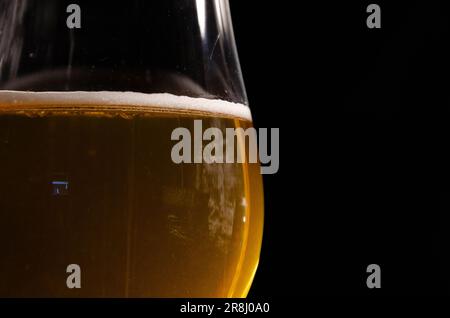 A glass mug containing an amber liquid sits on a dark surface ...