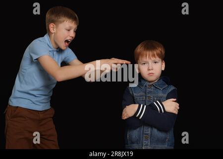 Boy laughing and pointing at upset kid on light grey background ...