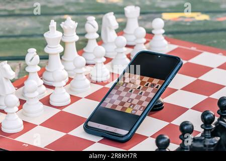 A chess app on a smartphone and a real chessboard with pieces on a ...