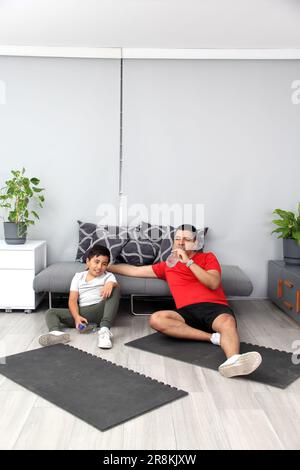 Latino dad and son take a break after exercising at home, drink water ...