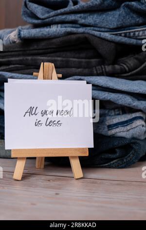 ALL YOU NEED IS LESS text on paper note on Jeans clothes assortment ...