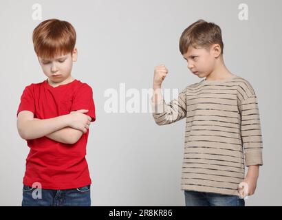 Boy with clenched fist looking at scared kid on light grey background ...