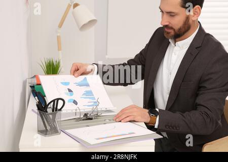 Businessman putting document into file folder at wooden table in office ...