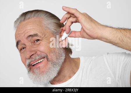Senior man using ear drops on white background Stock Photo - Alamy
