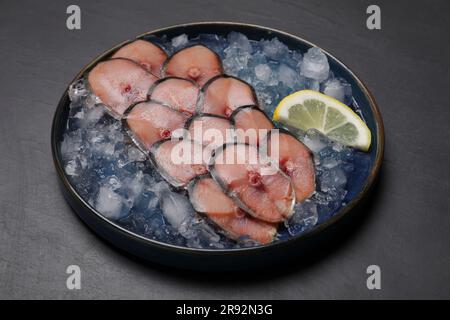 Raw mackerel slices, ice cubes and lemon served with vasabi on dark ...