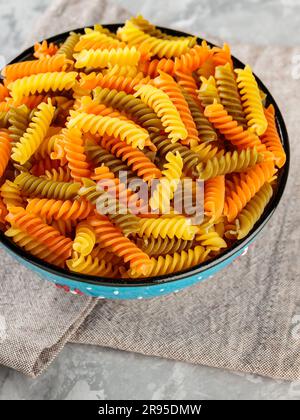 Multicolor spiral macaroni pasta in a wooden bowl on a red brown rustic ...
