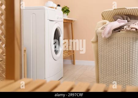 Laundry basket overfilled with clothes near washing machine in bathroom ...