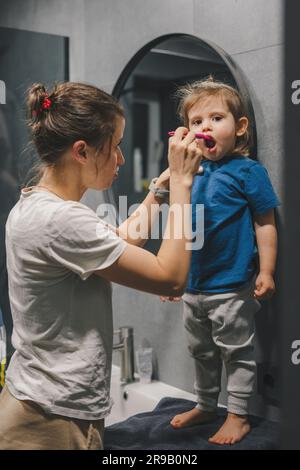 Mother brushing teeth to happy toddler baby boy. Mom woman brushes ...