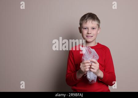 Happy boy popping bubble wrap on beige background, space for text ...