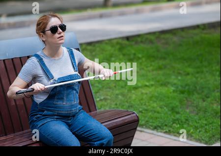 Blind pregnant woman folding walking stick while sitting on bench Stock ...