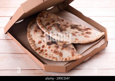 Cardboard box with delicious calzones on light wooden table, top view ...