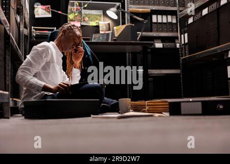 Overworked exhausted cop sitting on floor analyzing report in office ...